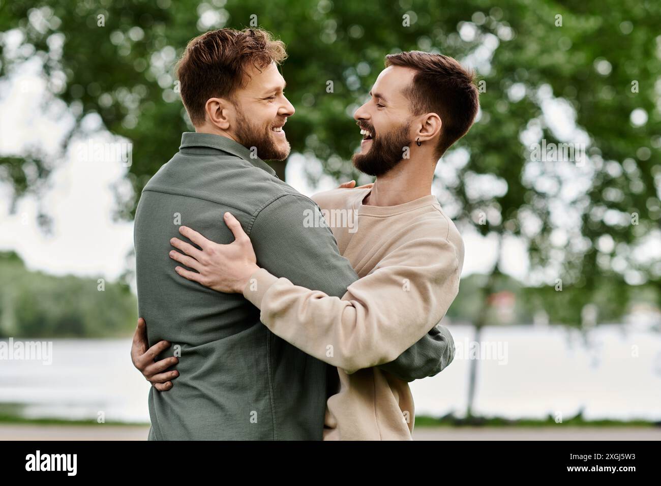 Two bearded men embrace in a park, laughing and looking at each other ...