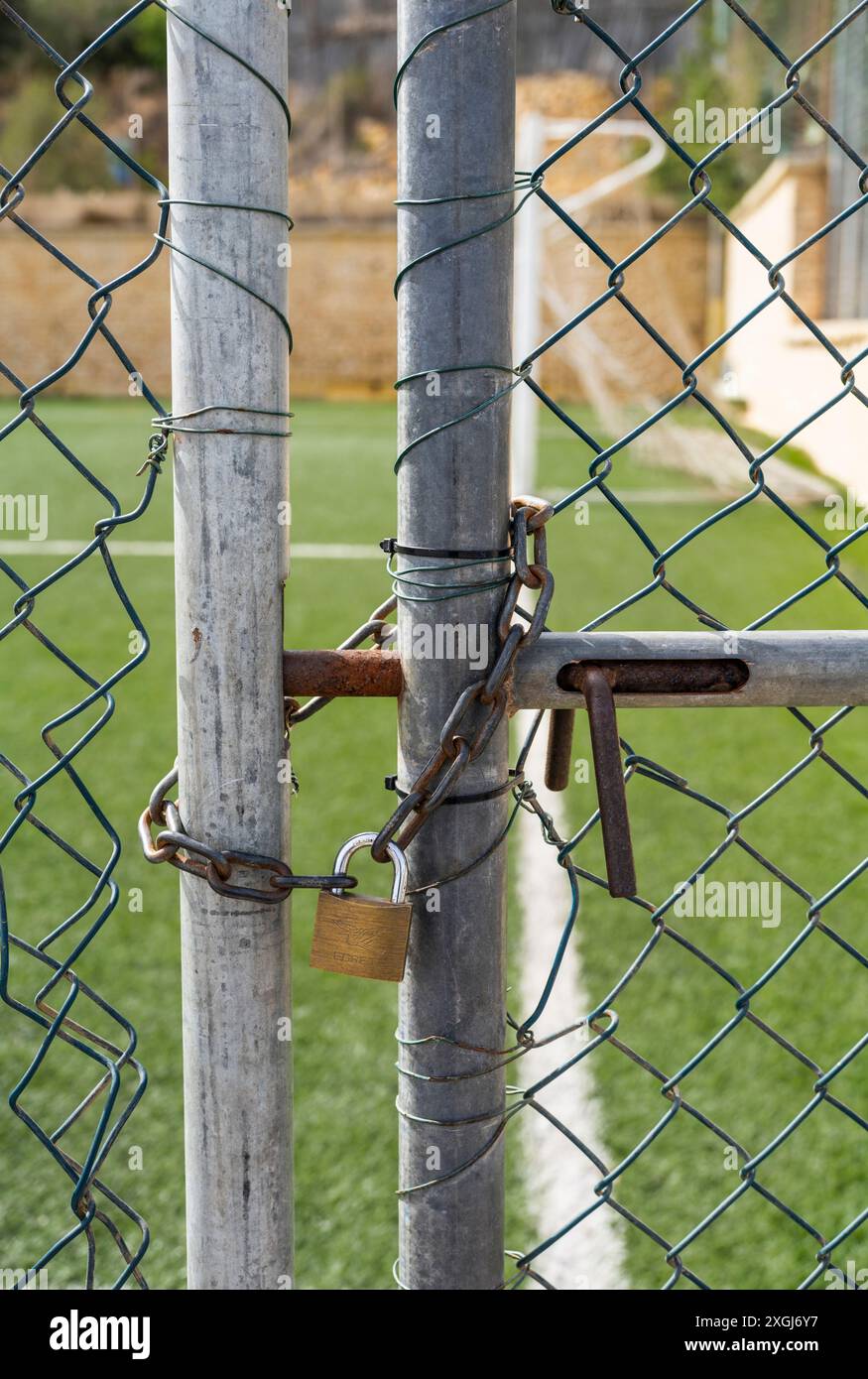 Close-up of a locked gate with a chain and padlock on a football field ...