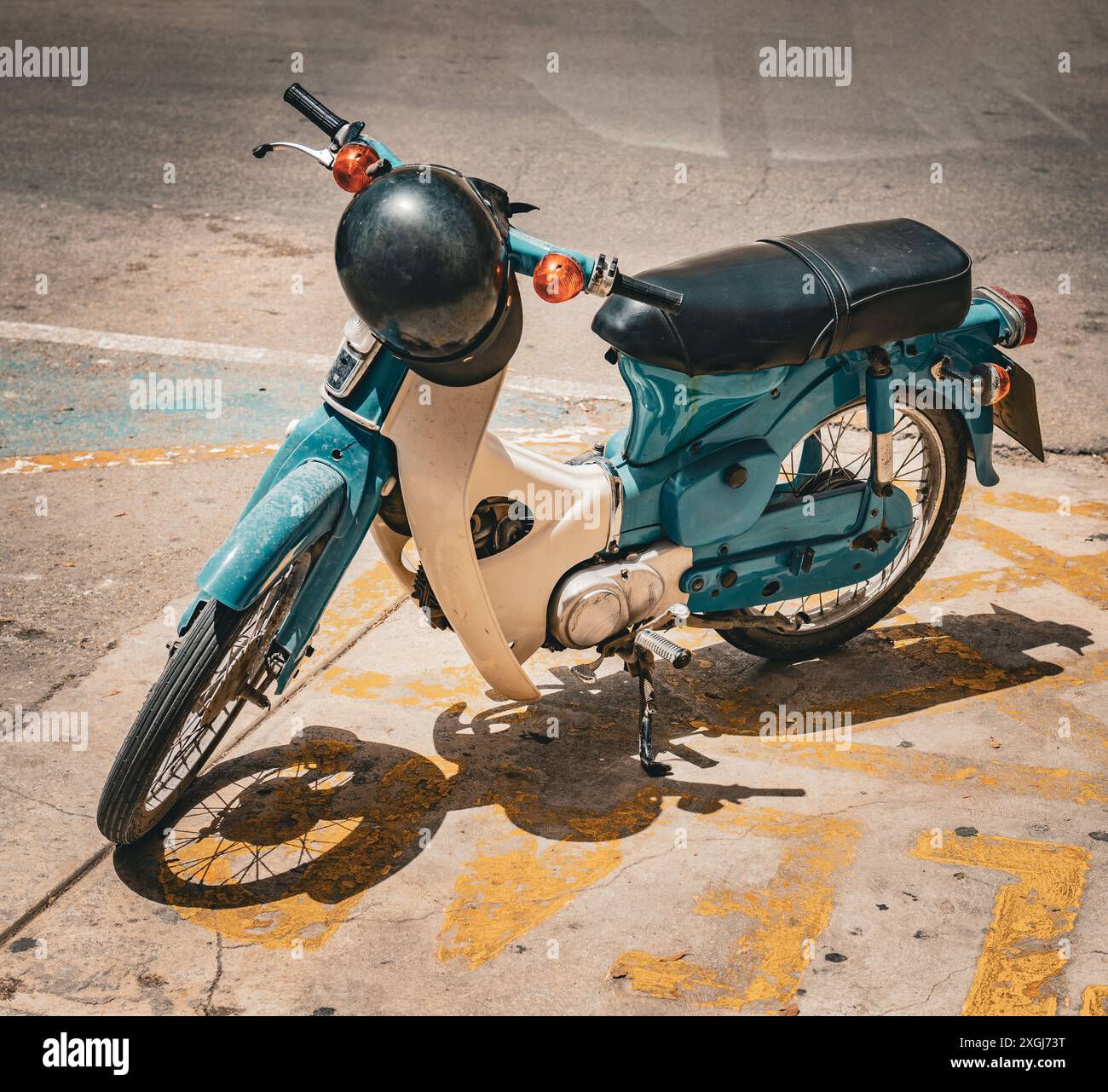 A vintage blue moped with a black helmet parked on an urban street ...