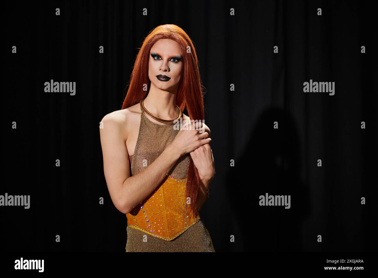 A drag queen poses in a glamorous gold and orange ensemble, her ...