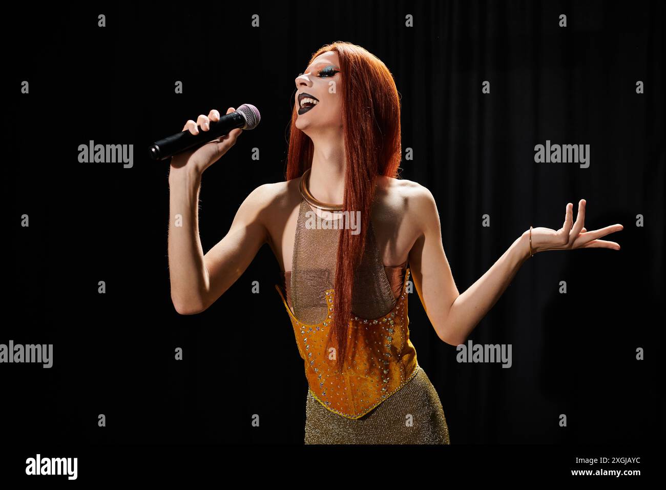 A drag diva in a sparkling gold gown performs on stage, microphone in ...