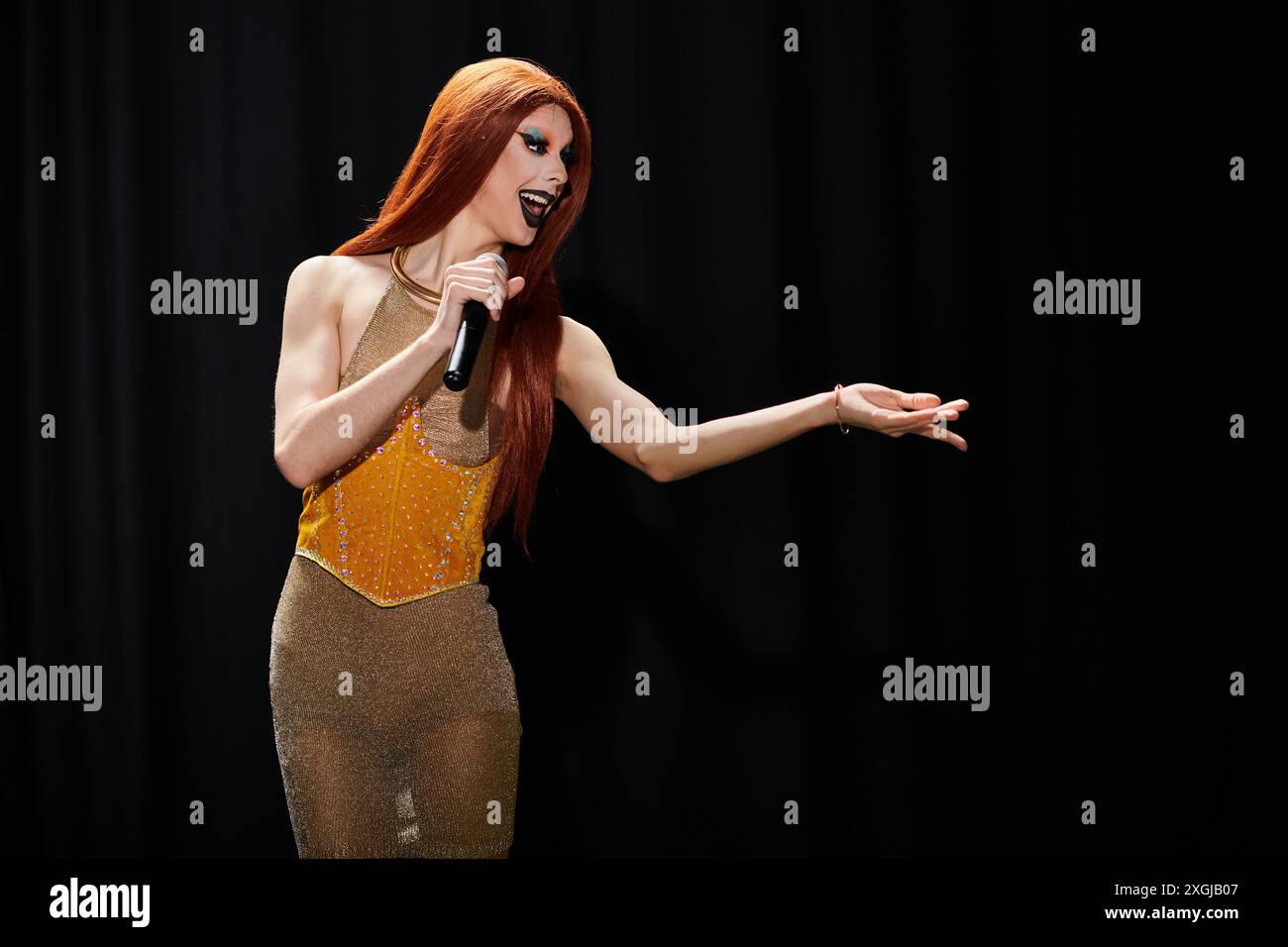 A drag performer in a glamorous outfit sings into a microphone on stage ...