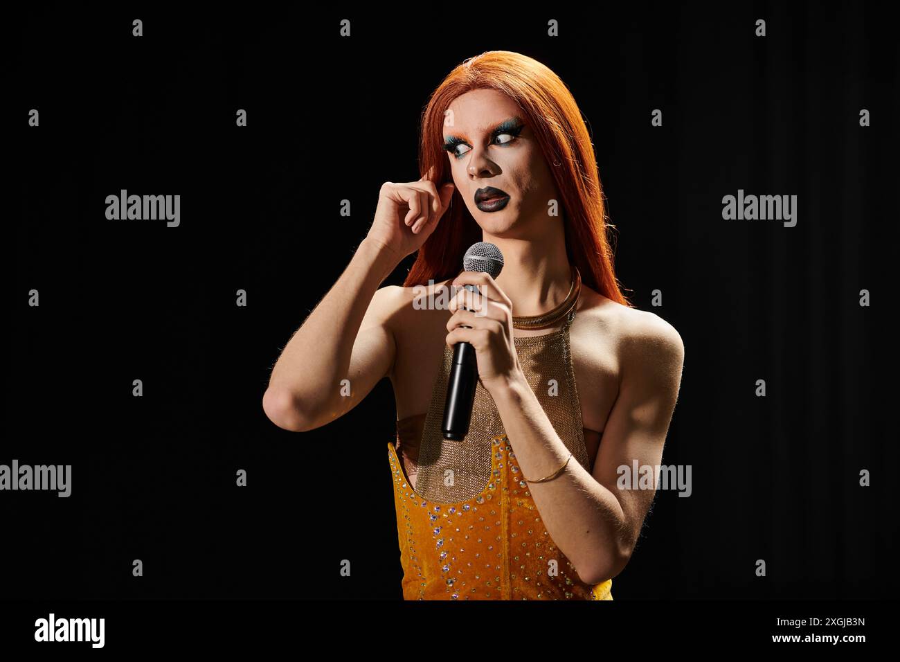 A drag queen with red hair and a glamorous outfit holds a microphone ...