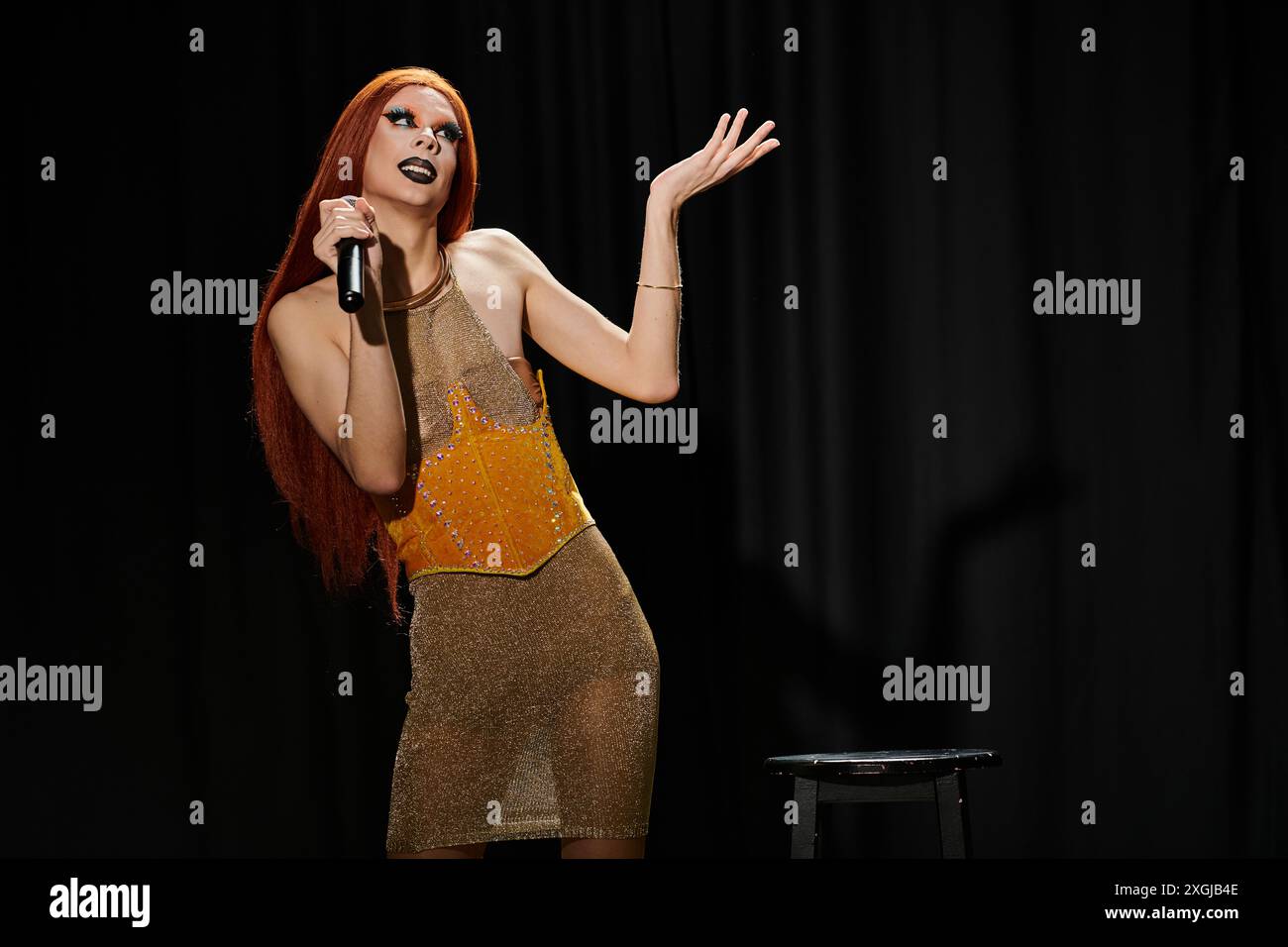 A drag performer in a shimmering gold dress holds a microphone and ...