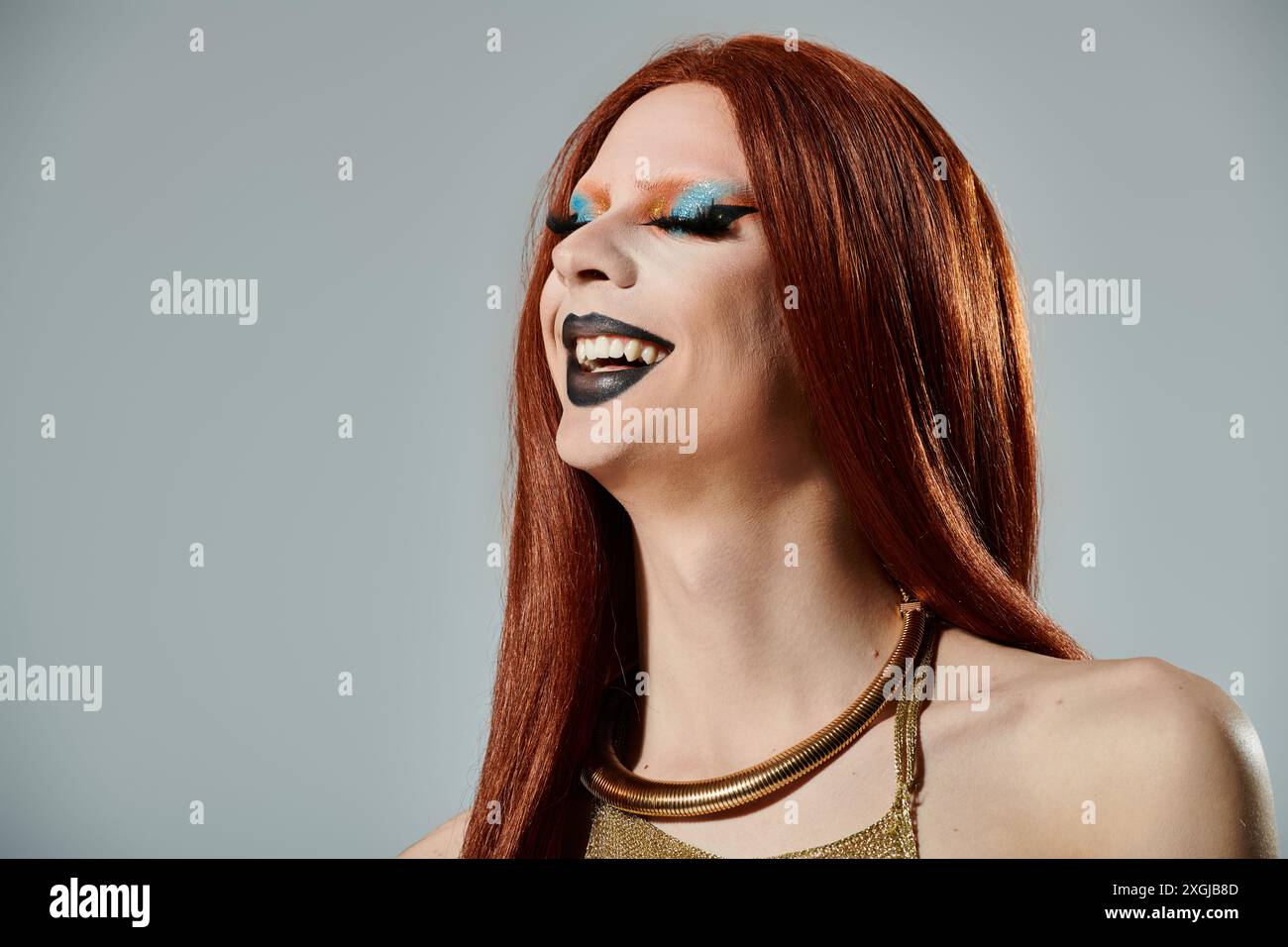 A drag queen with long red hair and colorful makeup laughs radiantly ...