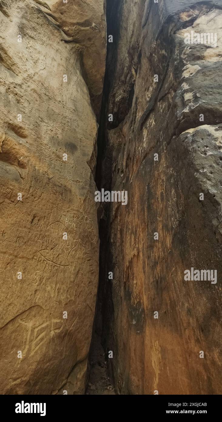 A narrow crack separates two large sandstone cliff faces. Vertical ...