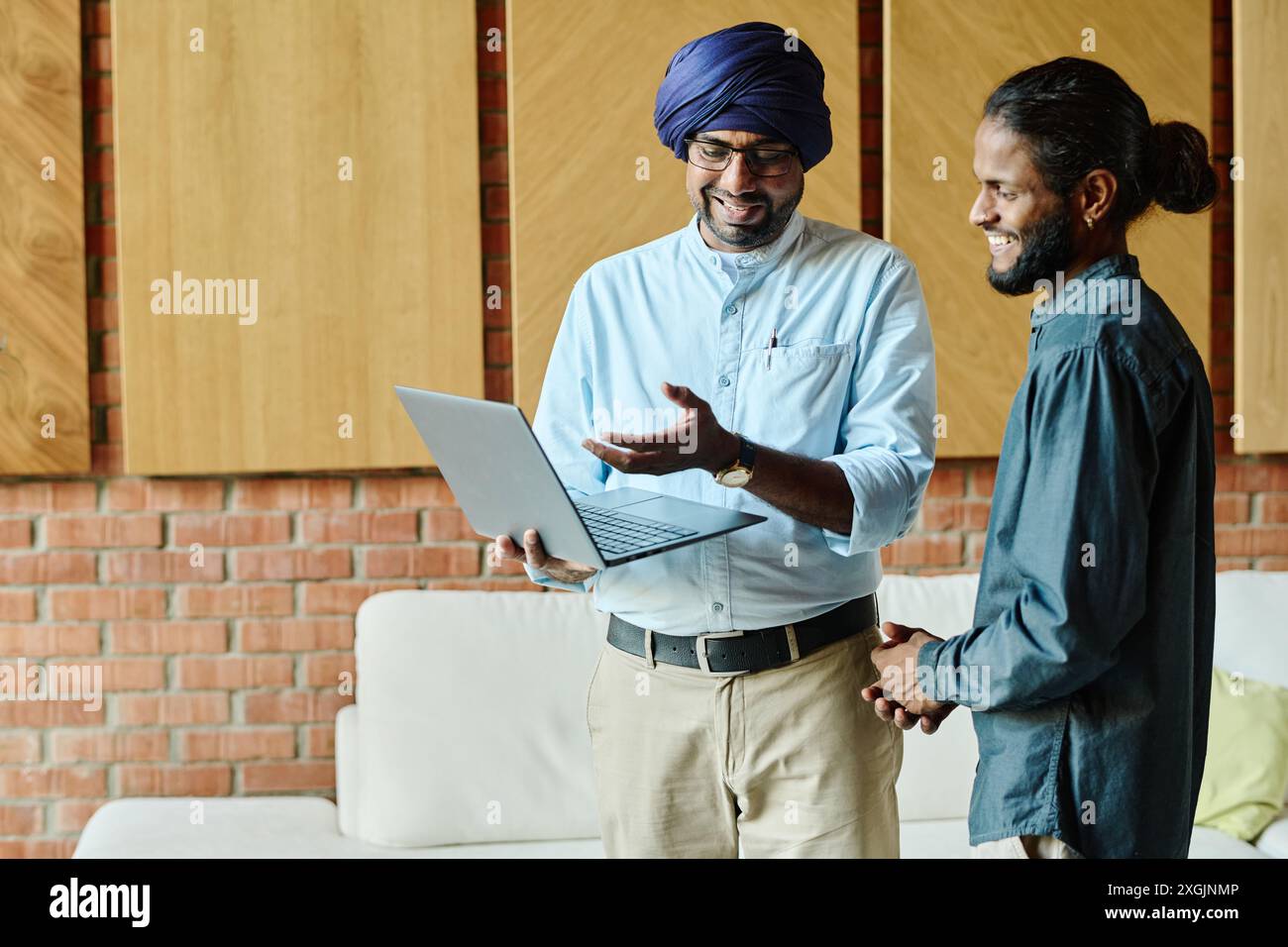 Two Indian colleagues standing in office waiting zone while one of them ...