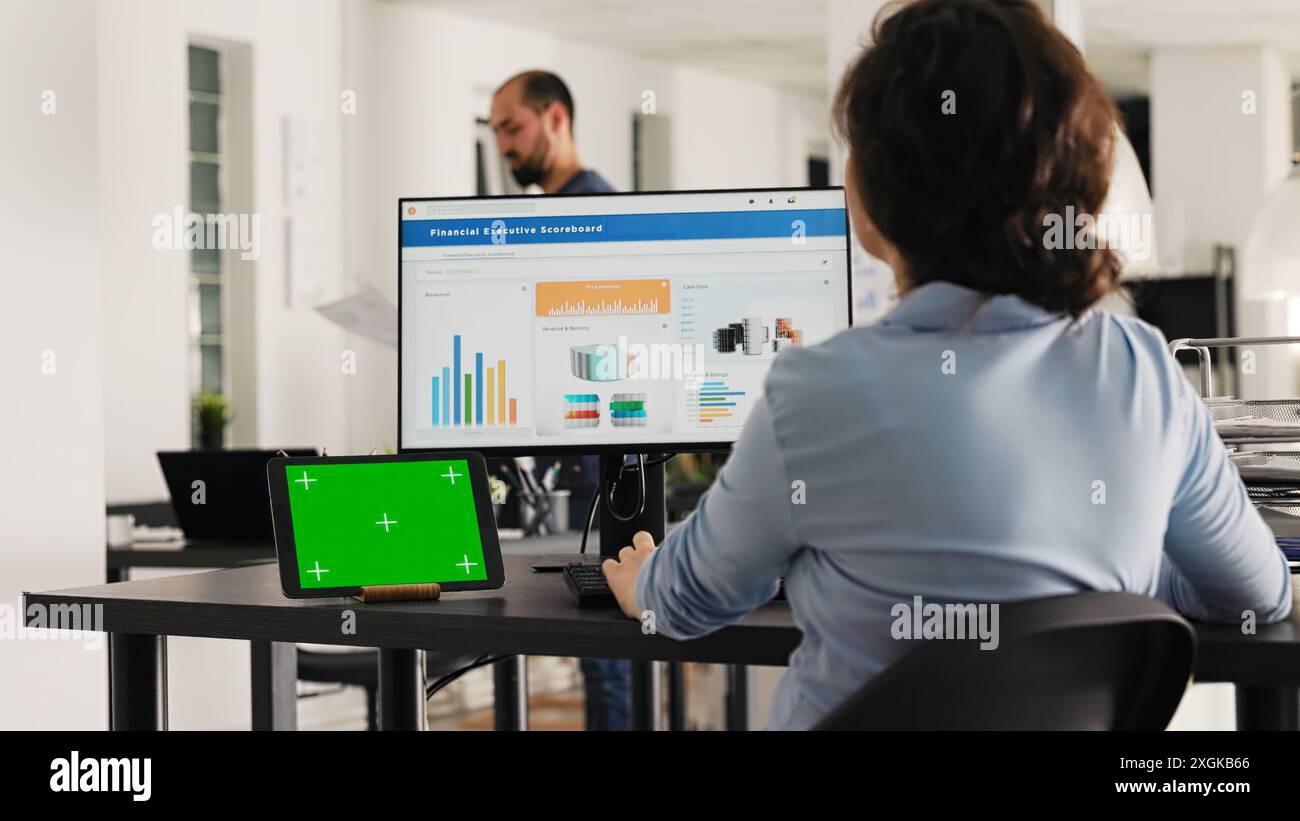 Analyst working at office desk with greenscreen shown on tablet ...