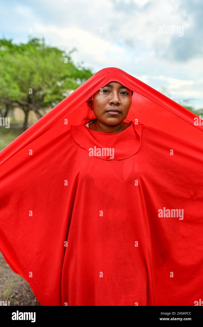 An indigenous Wayuu woman, adorned in traditional red attire, stands ...