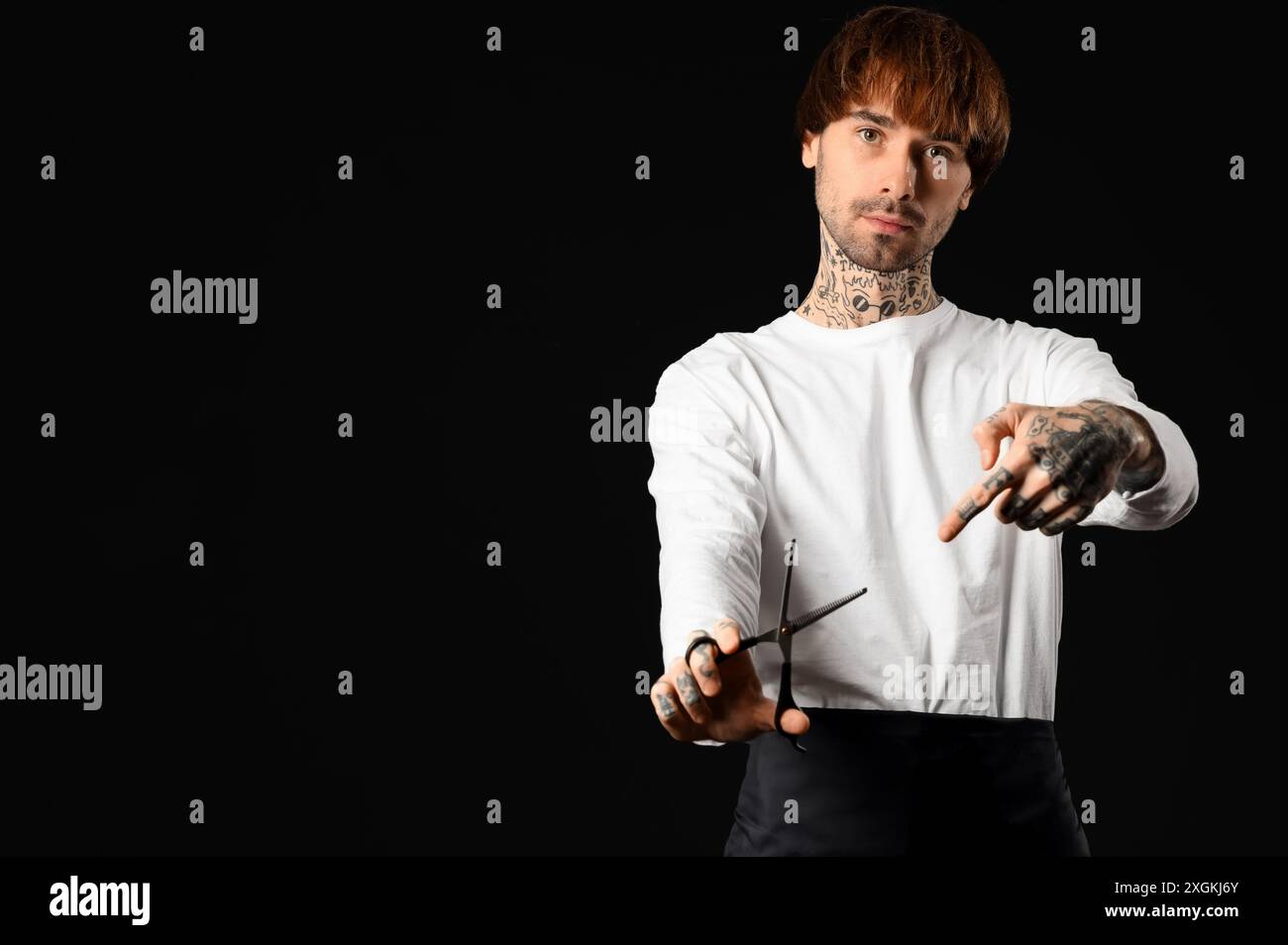 Young tattooed barber pointing at scissors on dark background Stock ...
