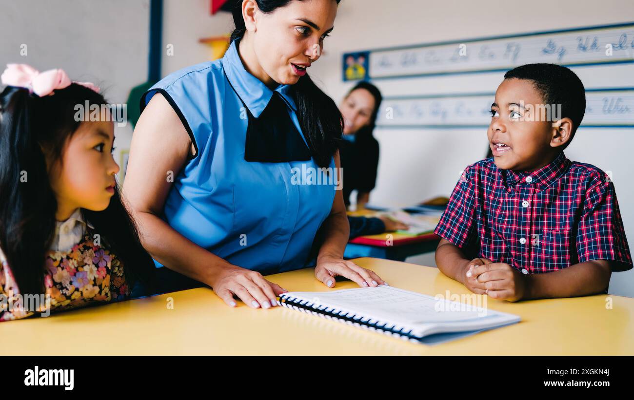 Teacher helping kid students learn to read in classroom at kindergarten ...