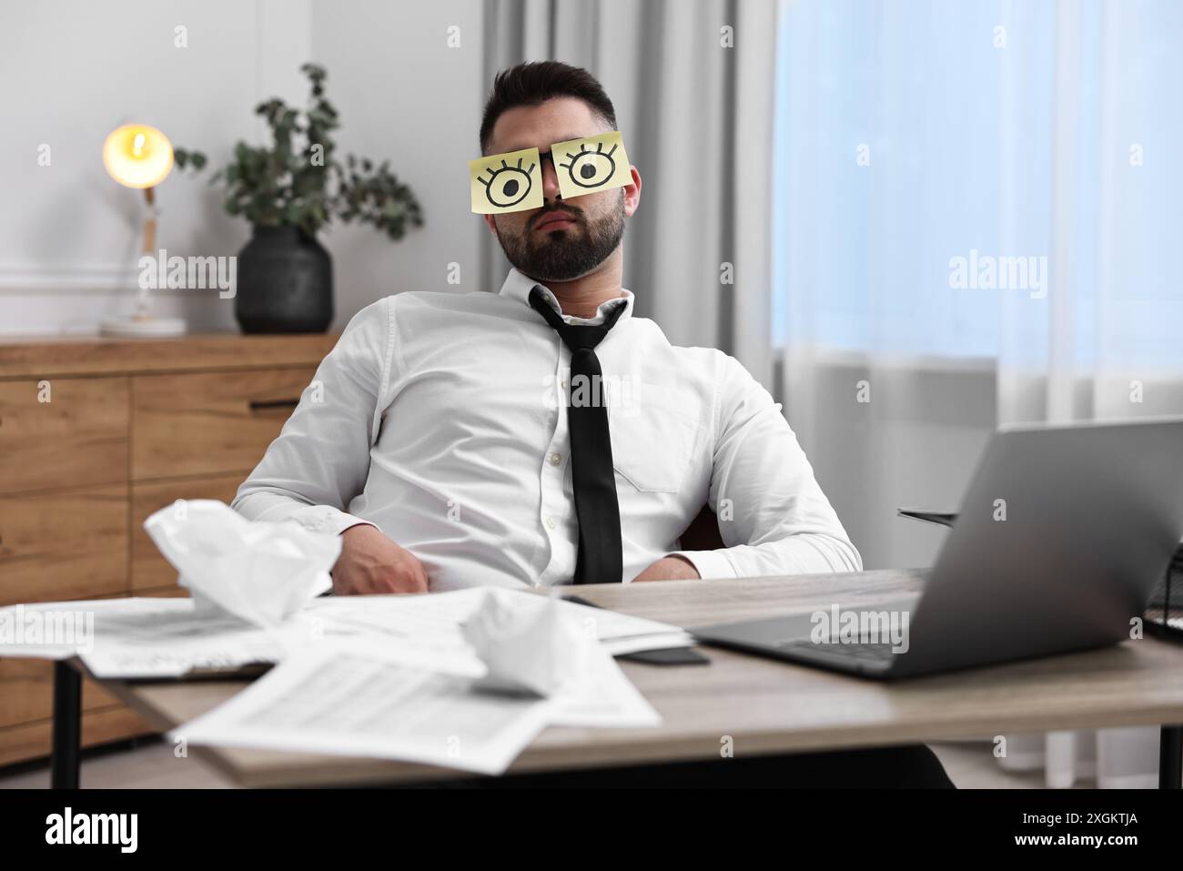 Man with fake eyes painted on sticky notes at workplace in office ...