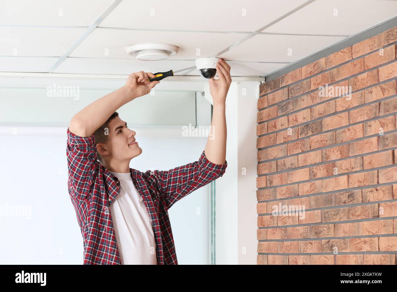 Technician with screwdriver installing CCTV camera on ceiling indoors ...