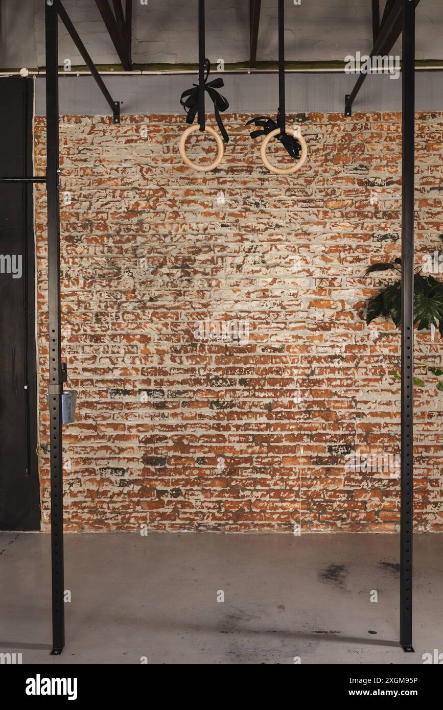 Gymnastic rings hang in a rustic indoor gym with a brick wall unaltered ...