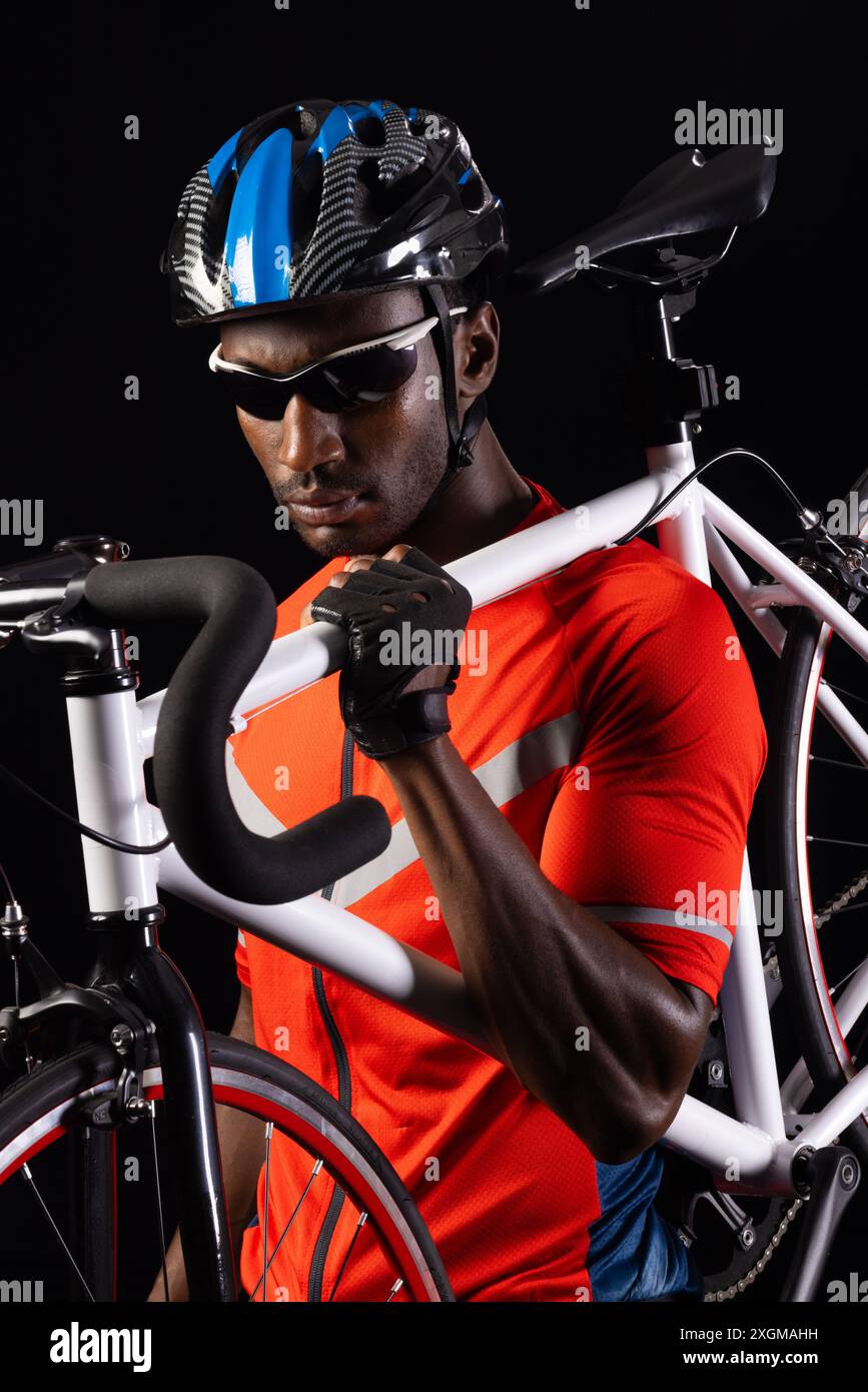 African American cyclist poses with his bike on a black background ...