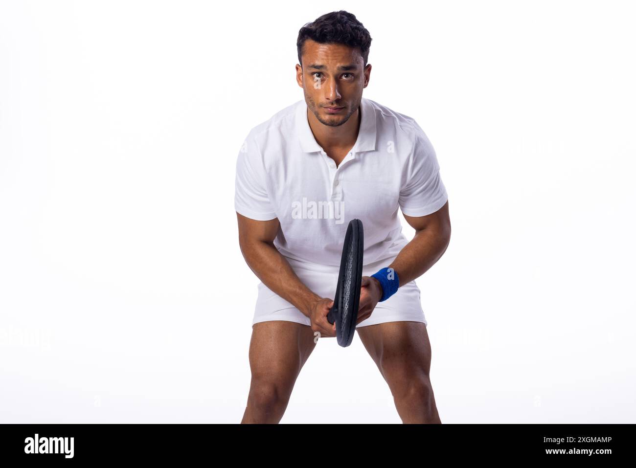 Young biracial man poised in tennis attire, ready for a match, on a white background. His ...