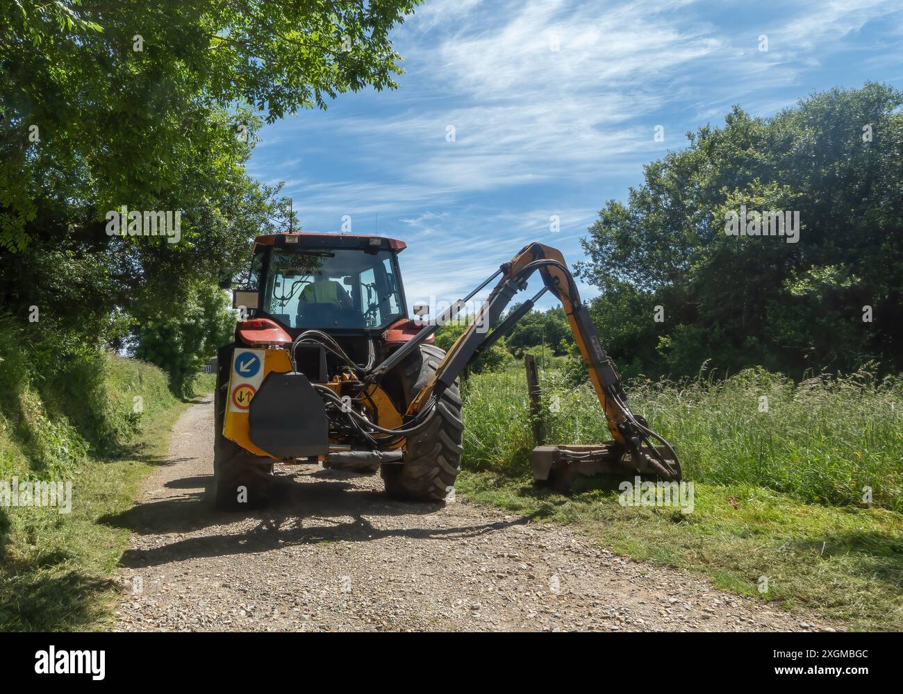 A tractor with a rotating blade attachment mows a hillside, leaving a ...