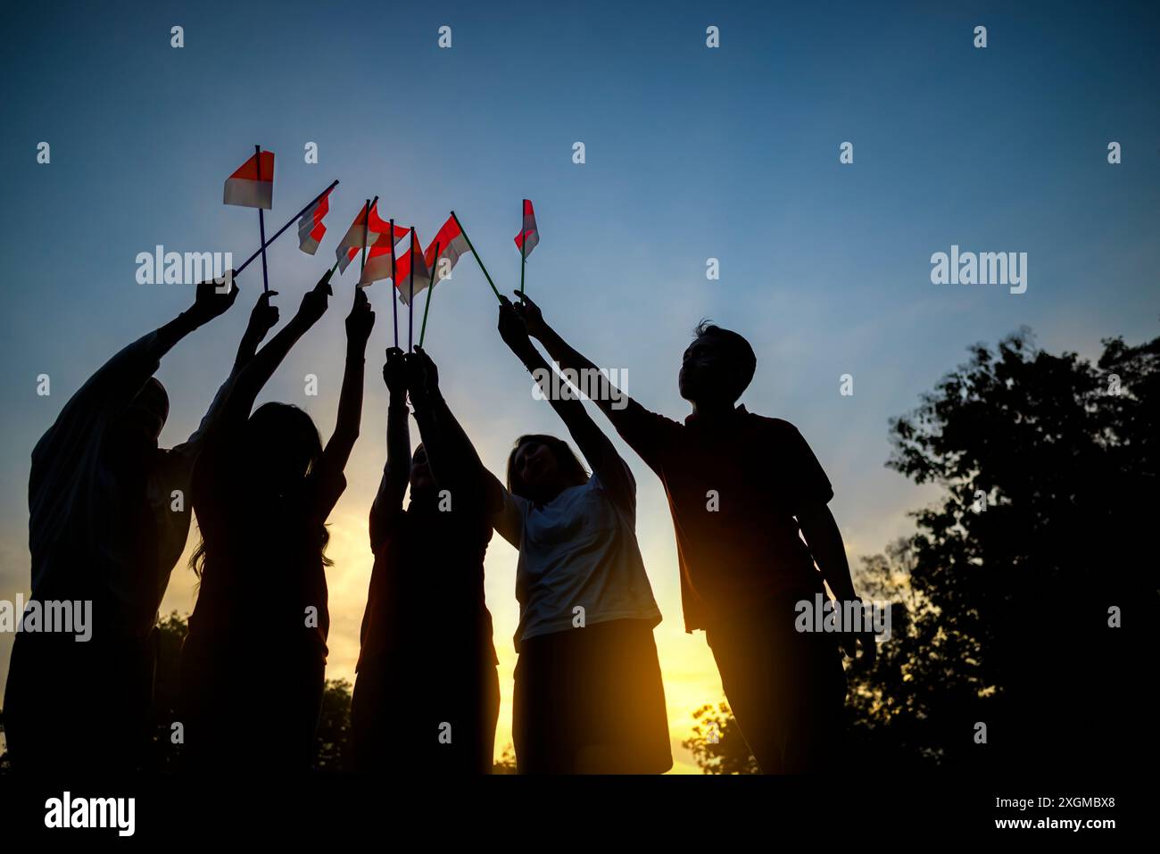 A silhouette of people raising small Indonesian flags outdoors with a ...