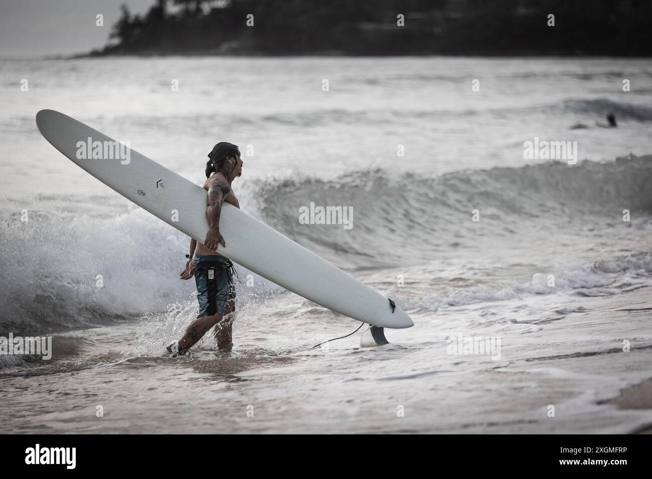 A surfer with his surfboard walking on the beach in Phuket Thailand ...