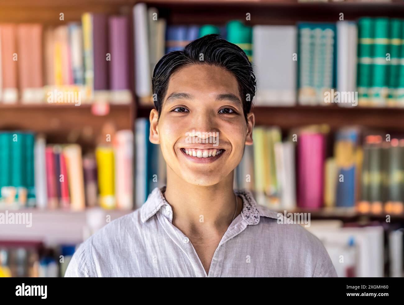 Smiling young Asian man in a library. He is standing in front of a ...