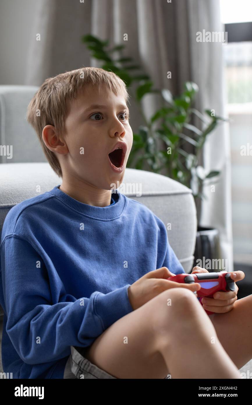 An astonished boy holds a game controller in hands, reacting to a video ...