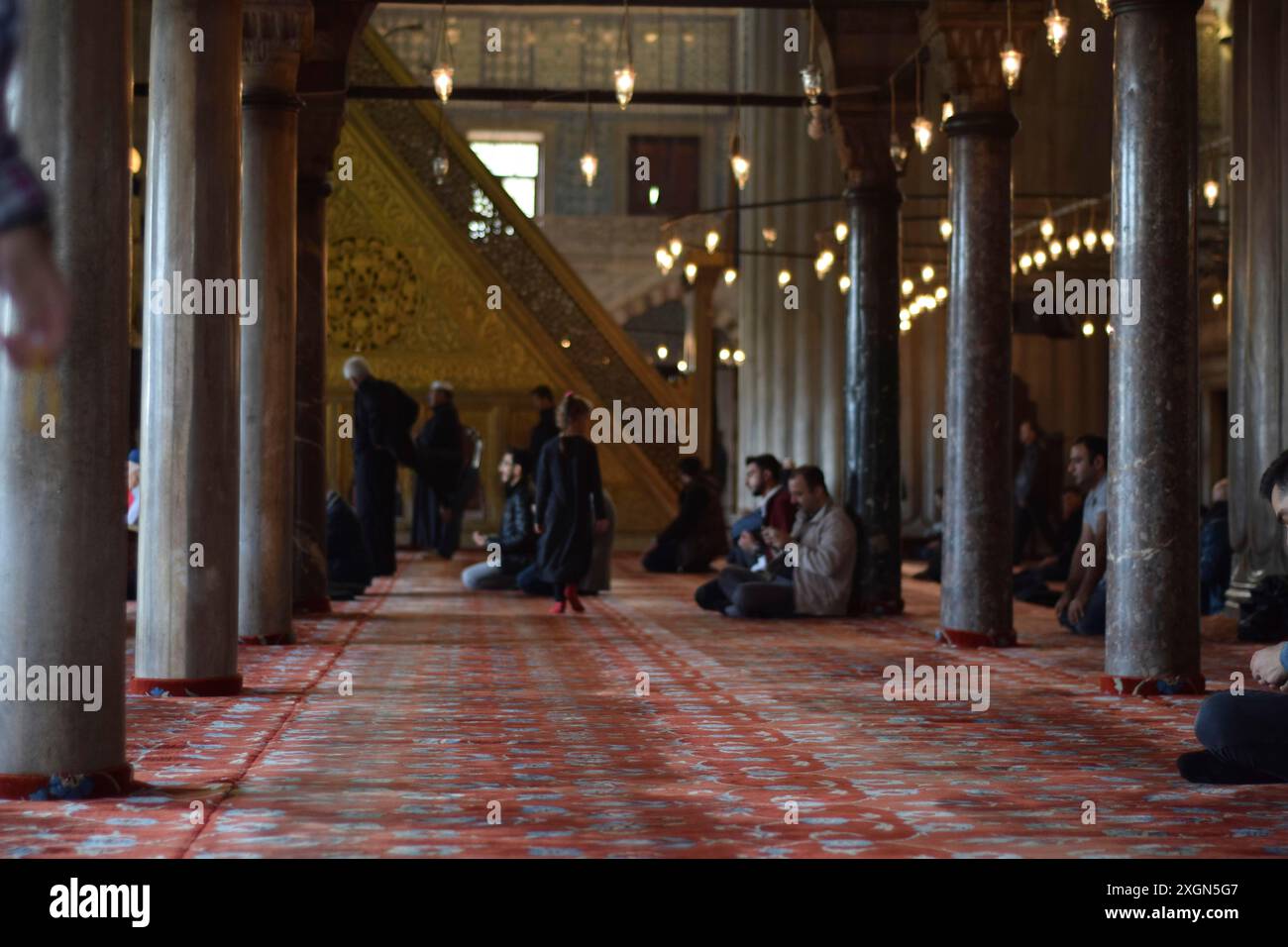Interior of a mosque with people in prayer, lit columns, and patterned ...