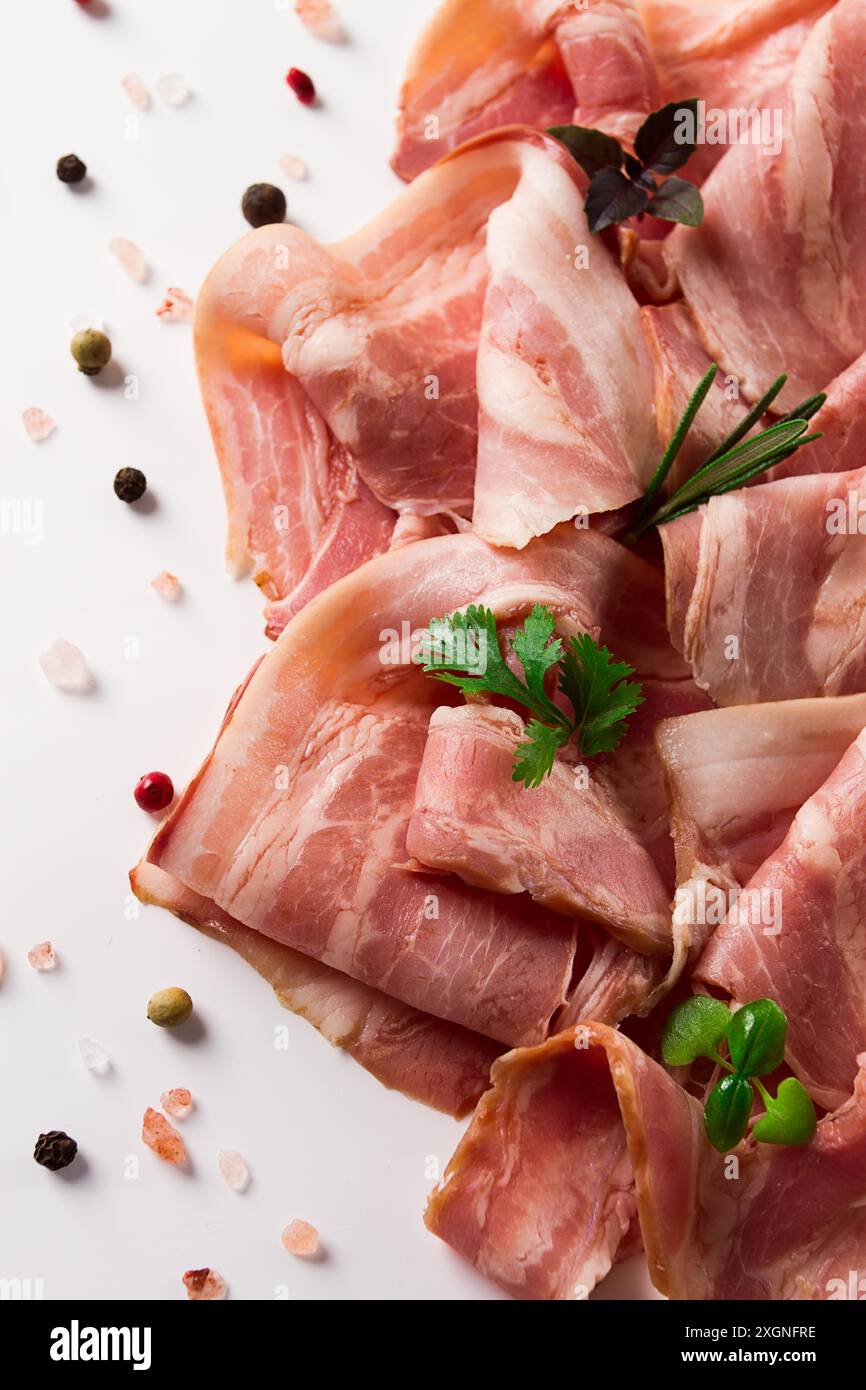 Raw bacon, sliced, with micro greenery and spices, on a white ...