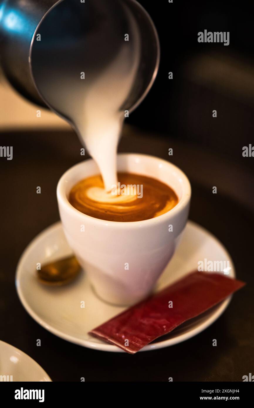 Milk pitcher pouring cream into a coffee cup. Vertical Stock Photo - Alamy
