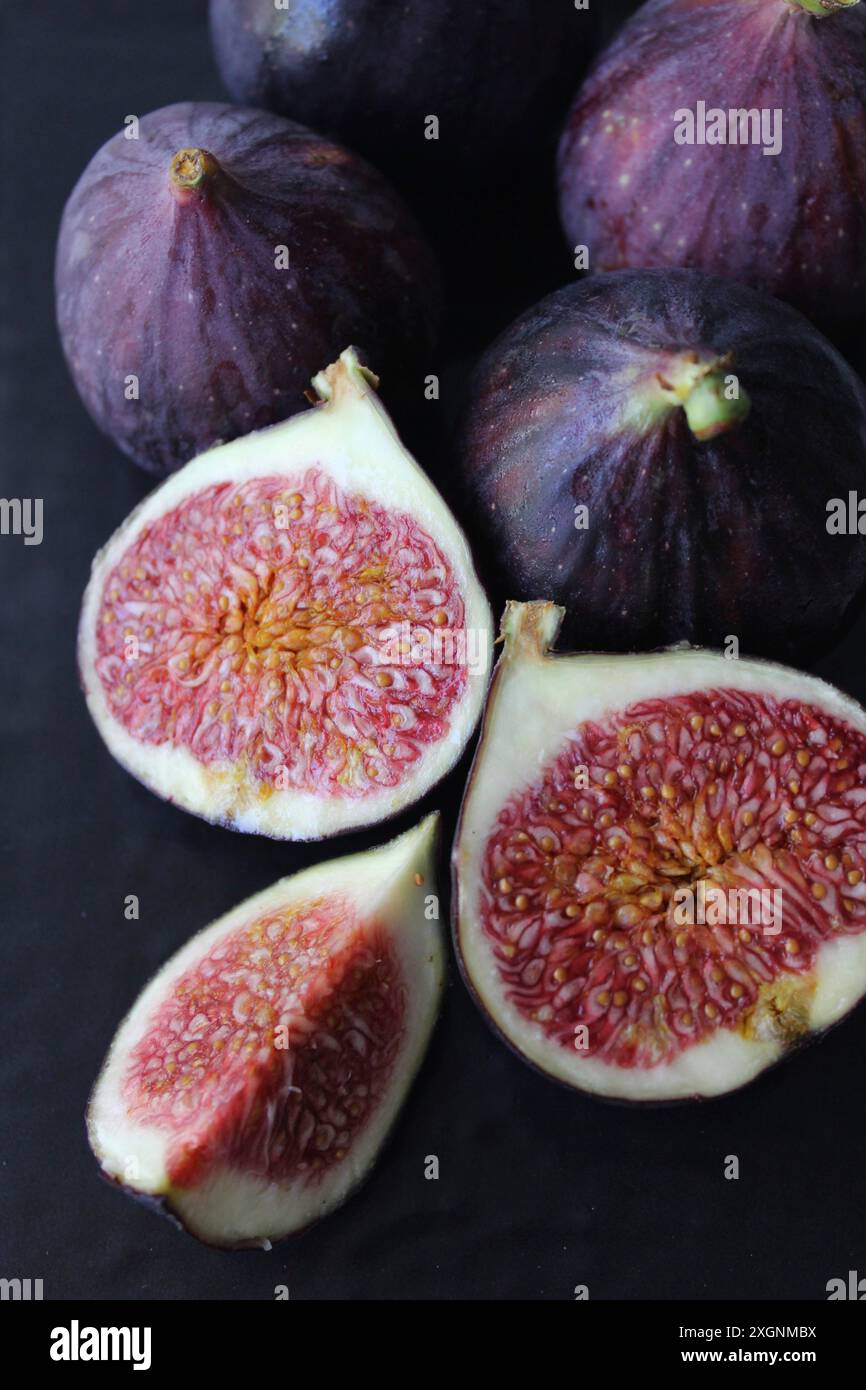 Several figs on a dark background, with some sliced open to reveal ...