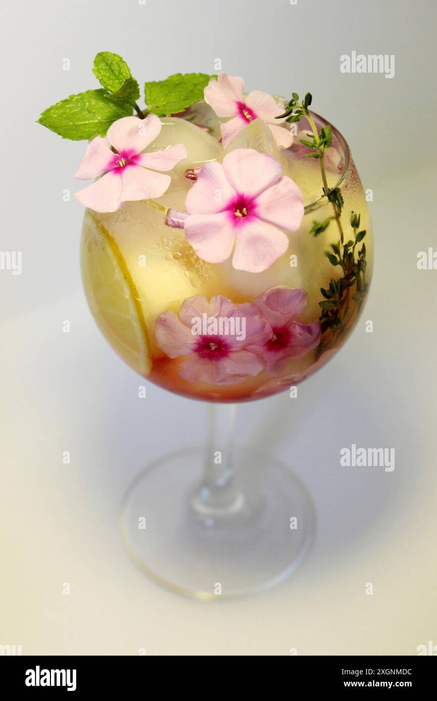 Elegant cocktail garnished with pink flowers, mint leaves, and a lemon ...