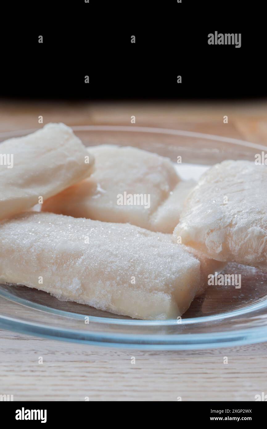 Frozen haddock fillets defrosting on a glass plate. On a wooden ...