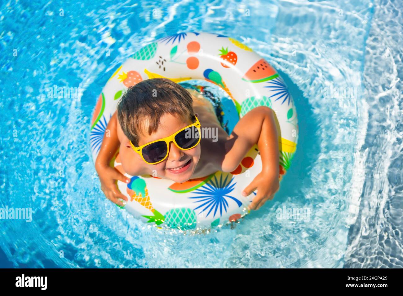 Top view of a cute boy in sunglasses playing in the swimming pool alone ...