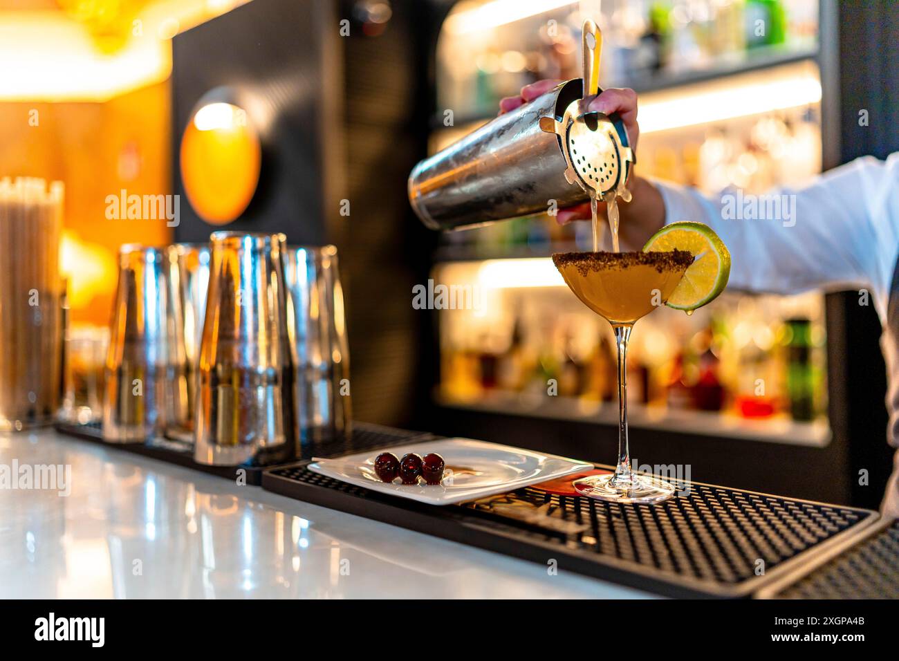 Hand of a waiter pouring cocktail into martini glass garnished with ...