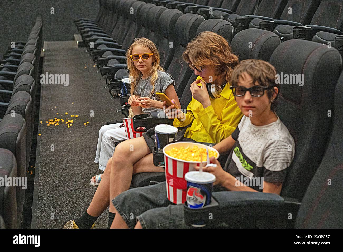 children sit in the cinema hall wearing 3D glasses with popcorn and a ...