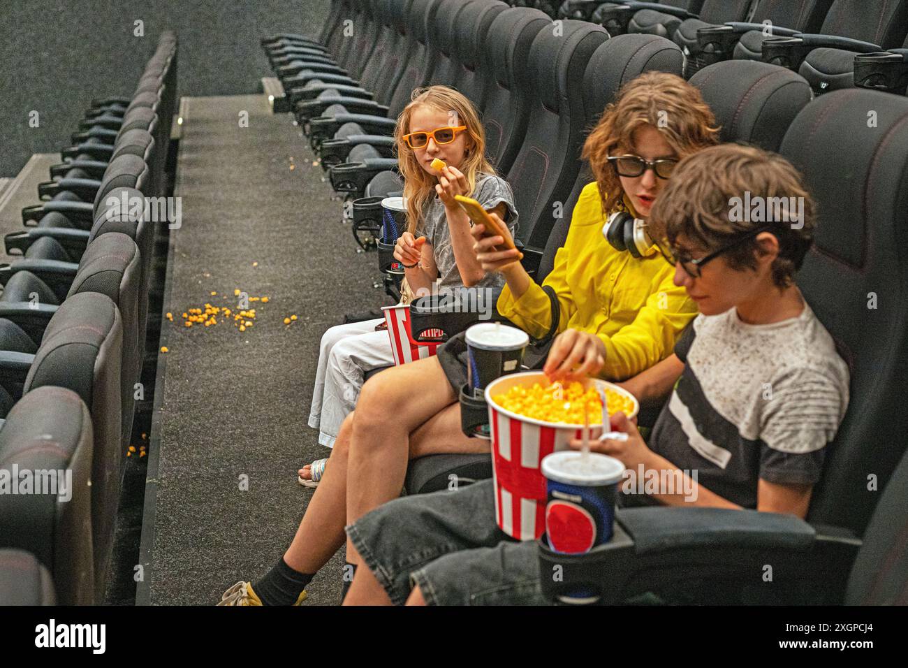 children sit in the cinema hall wearing 3D glasses with popcorn and a ...