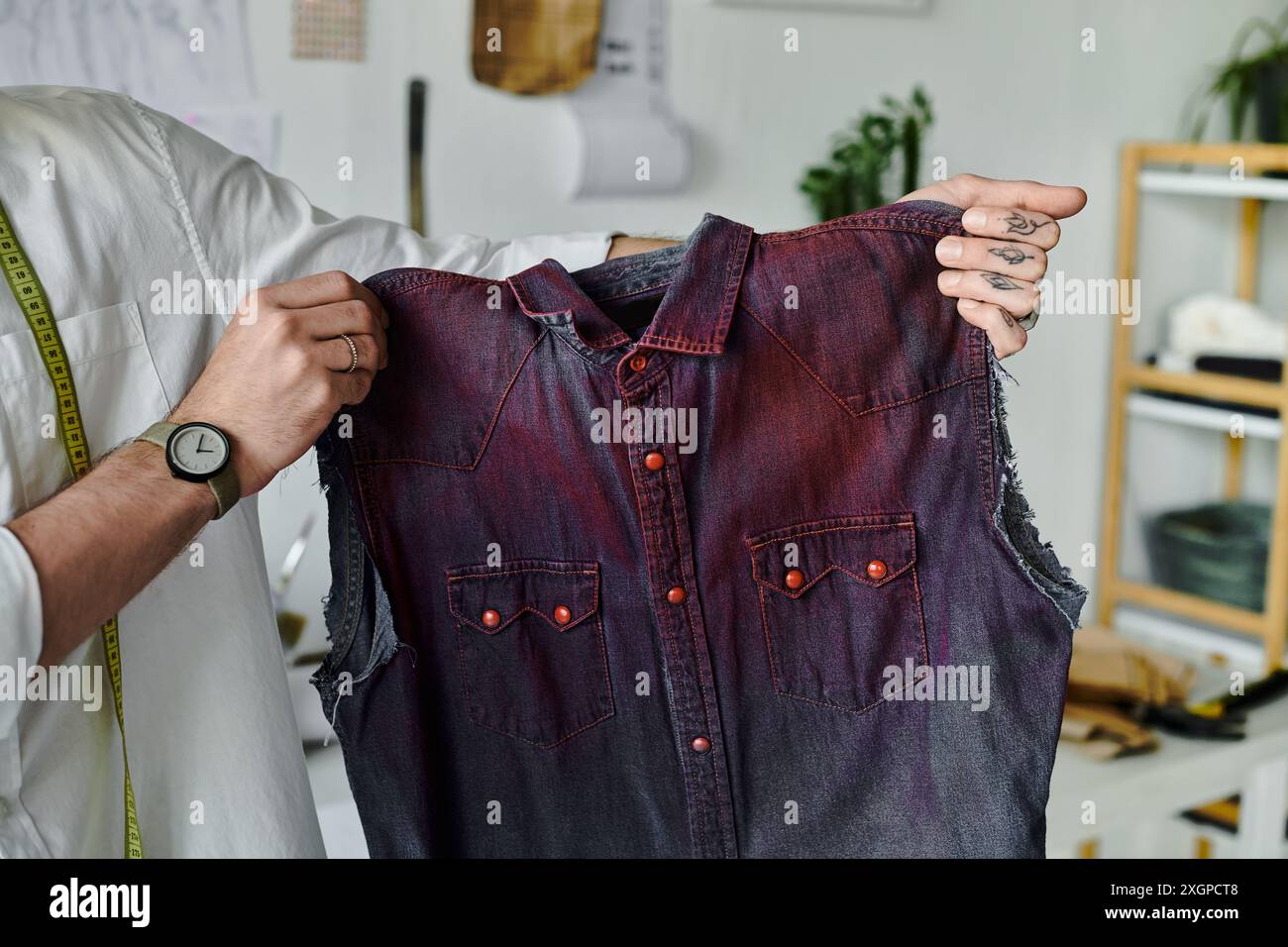 A young man holds up a restored denim shirt in his clothing restoration ...