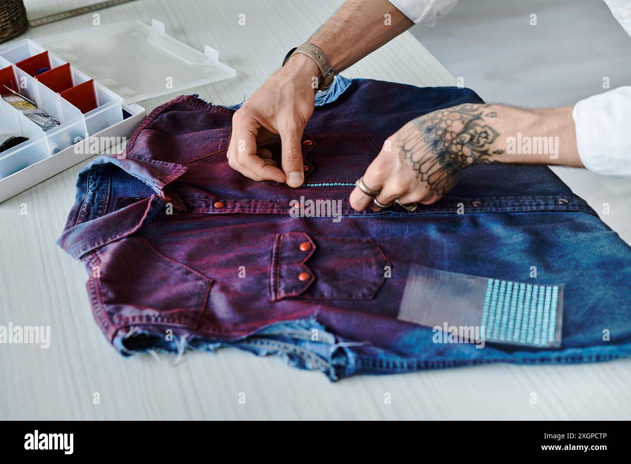 A young man with tattoos works on a discarded denim shirt, giving it ...