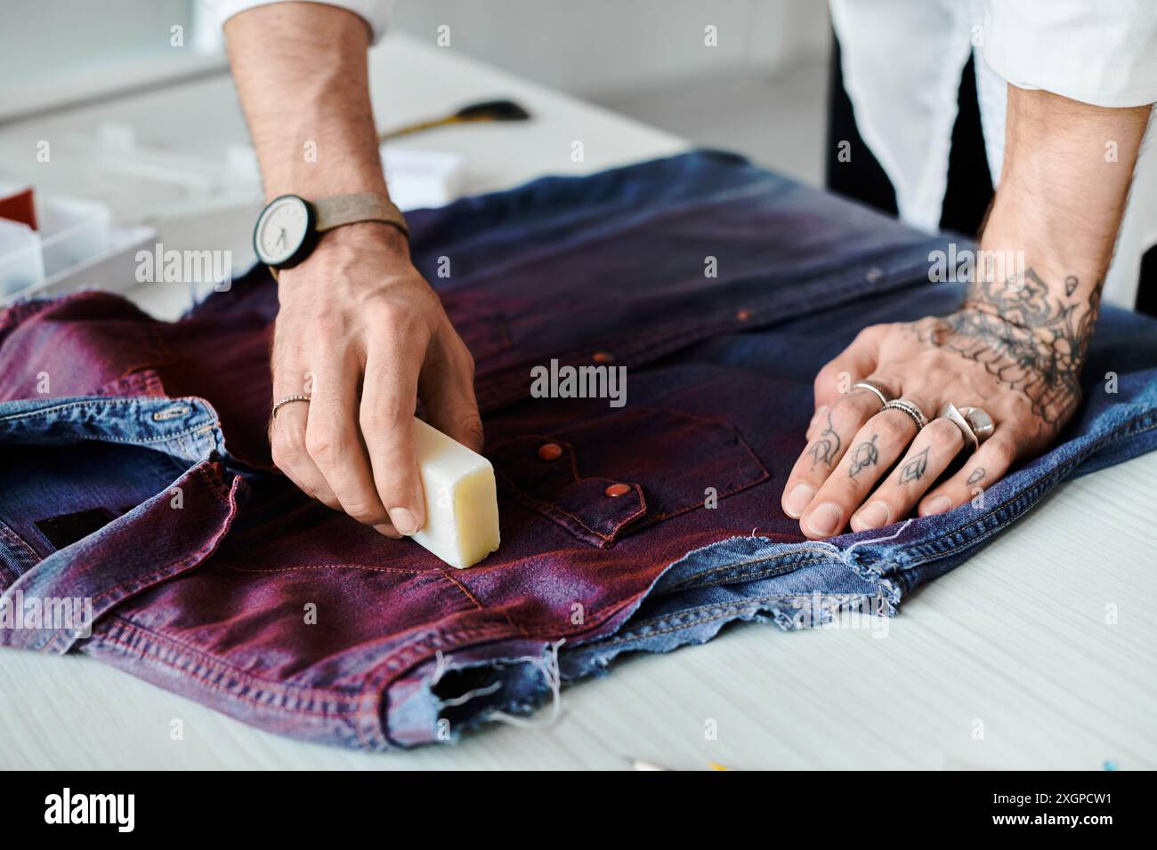 A young man restores a worn denim shirt in his DIY clothing atelier ...