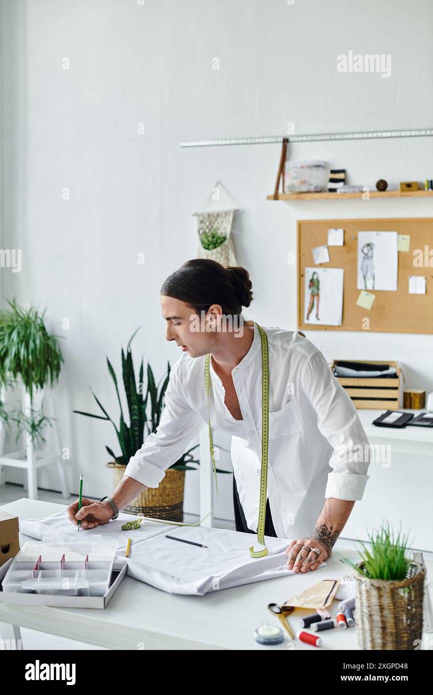 A young tailor, dressed in a white shirt, works on a clothing project ...