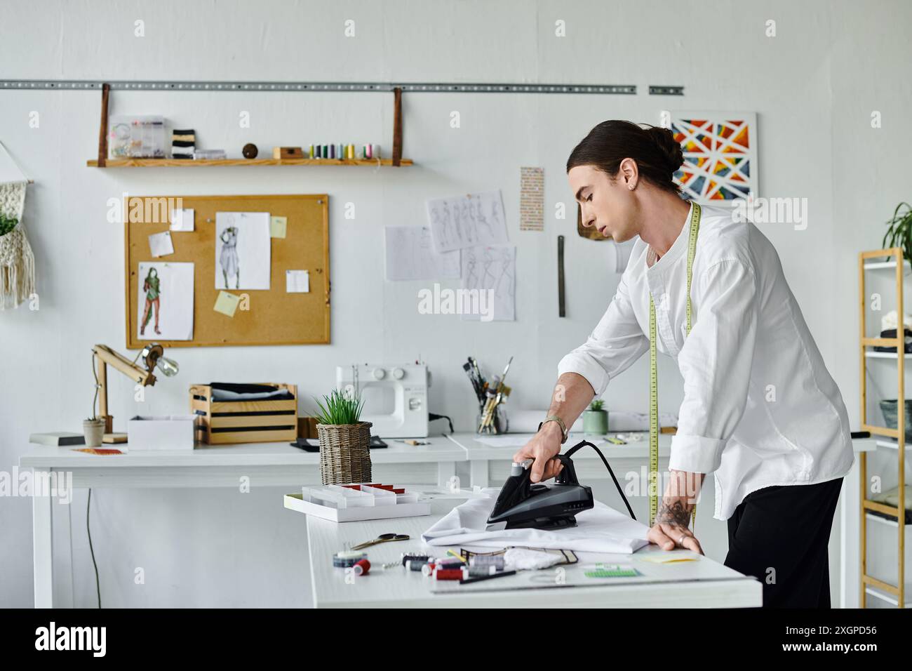 A young tailor in a white shirt carefully irons a garment in his DIY ...