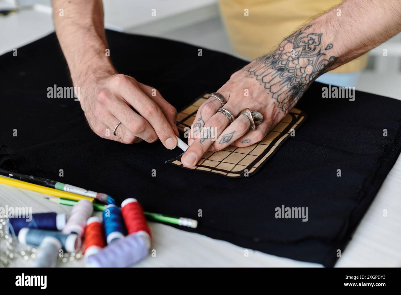A man with a heavily tattooed hand marks a piece of fabric with a chalk ...