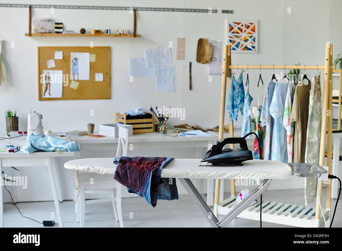 A white-walled atelier featuring a sewing machine, an ironing board ...