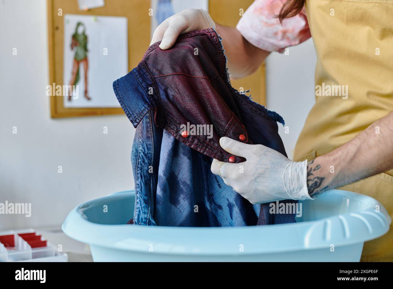 A young man dyes a denim jacket in his sustainable clothing restoration ...
