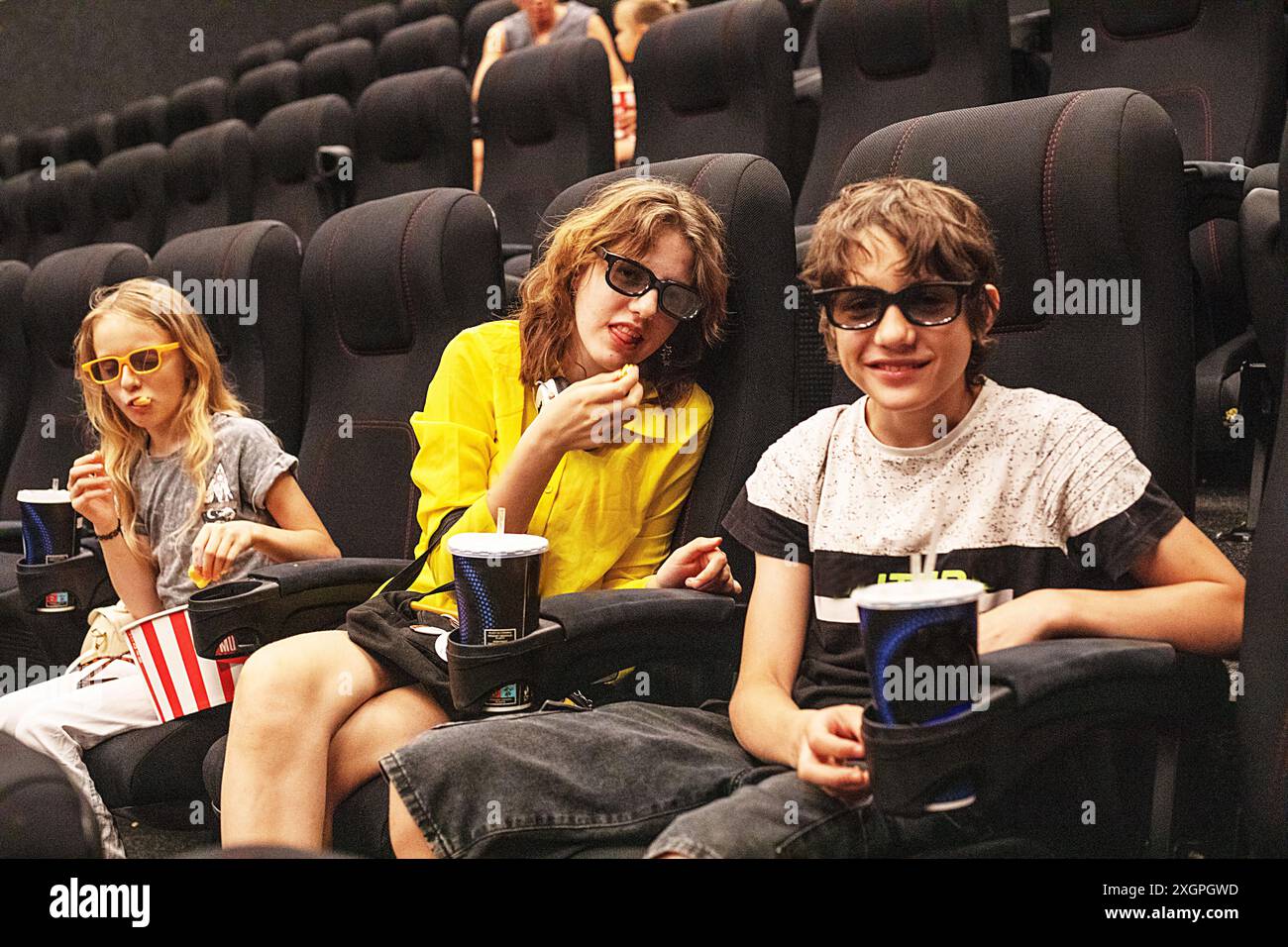 children sit in the cinema hall with popcorn before watching. family ...
