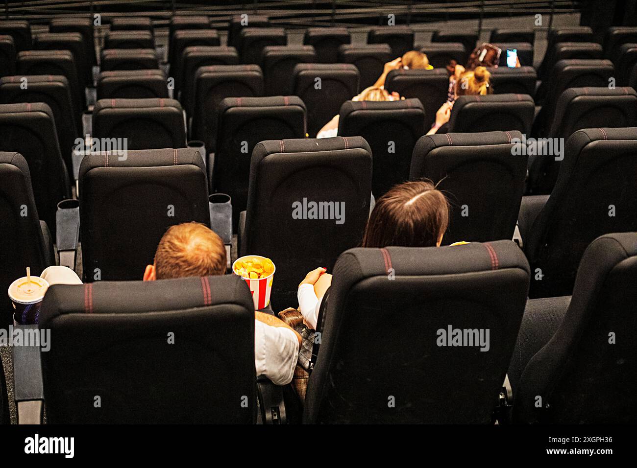 moviegoers sit in the cinema hall with popcorn before watching. family ...