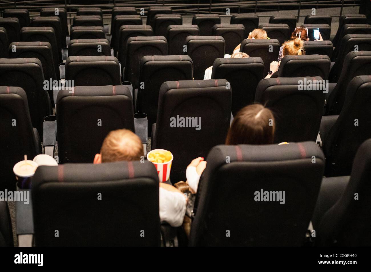 moviegoers sit in the cinema hall with popcorn before watching. family ...