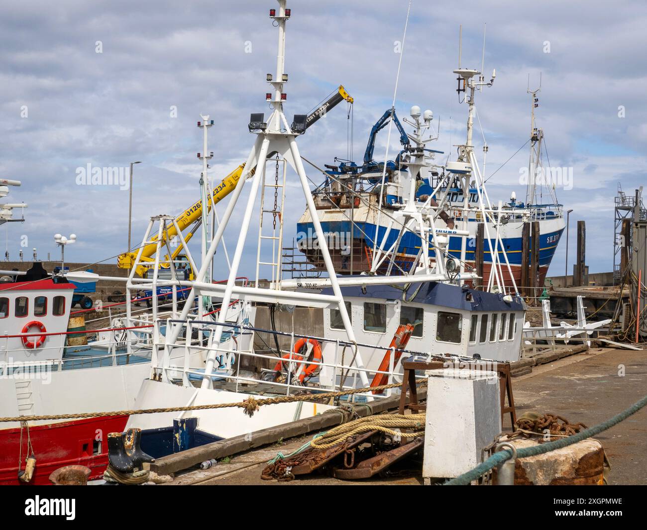 A crane and fishing trawlers in the harbour, at Macduff in ...