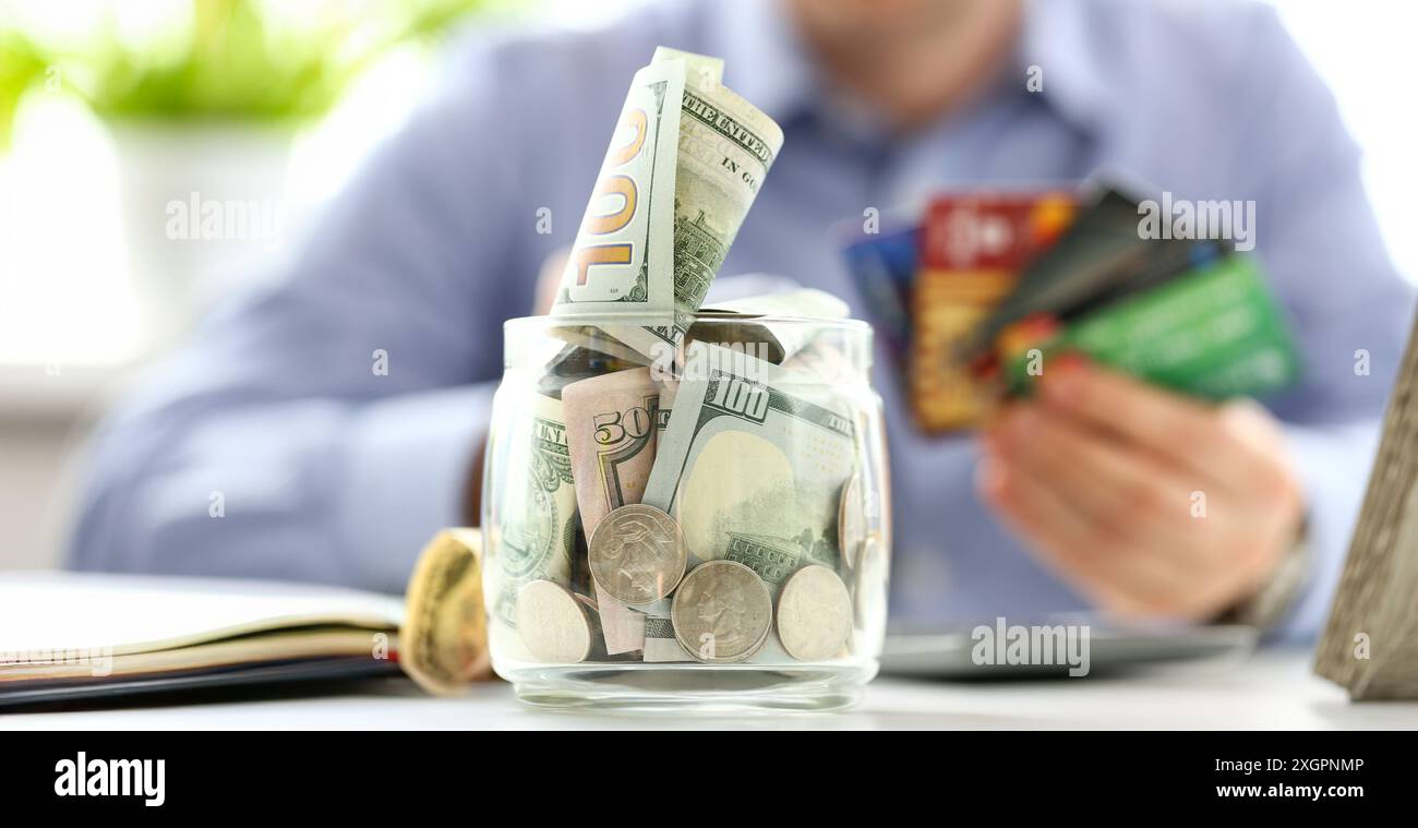 Big jar full of money stand at working table with male hand holding ...