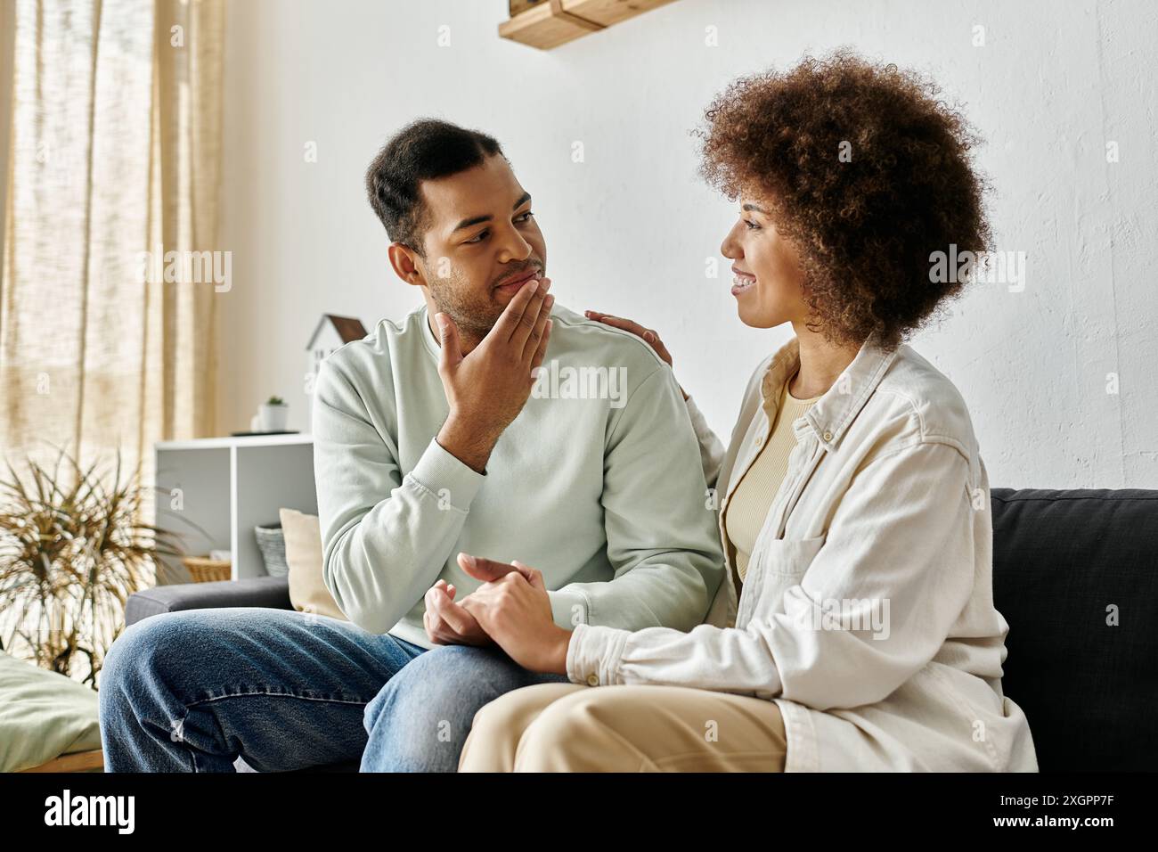 An African American couple sits on a couch at home, using sign language ...