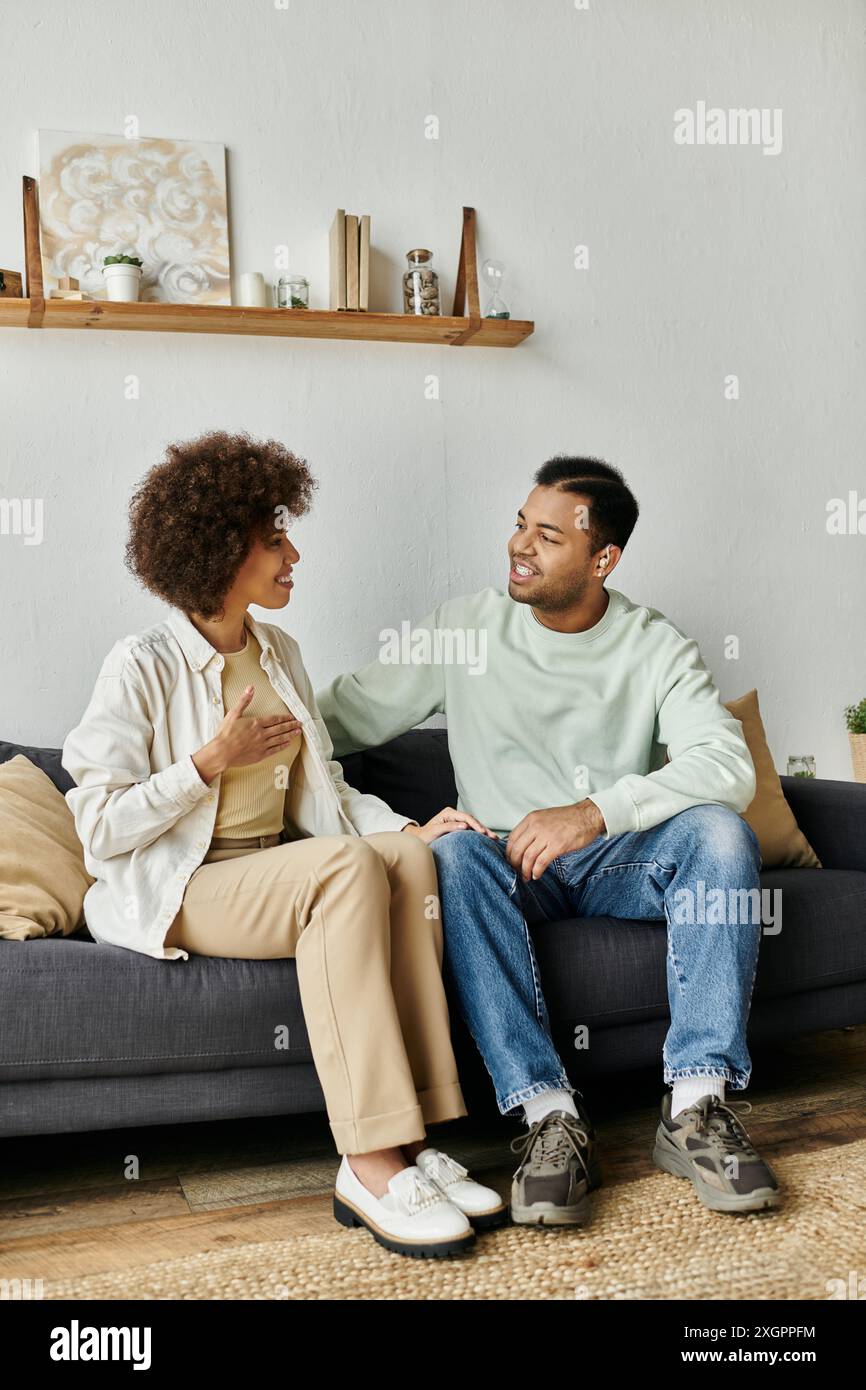 An African American couple sits on a couch at home, communicating ...